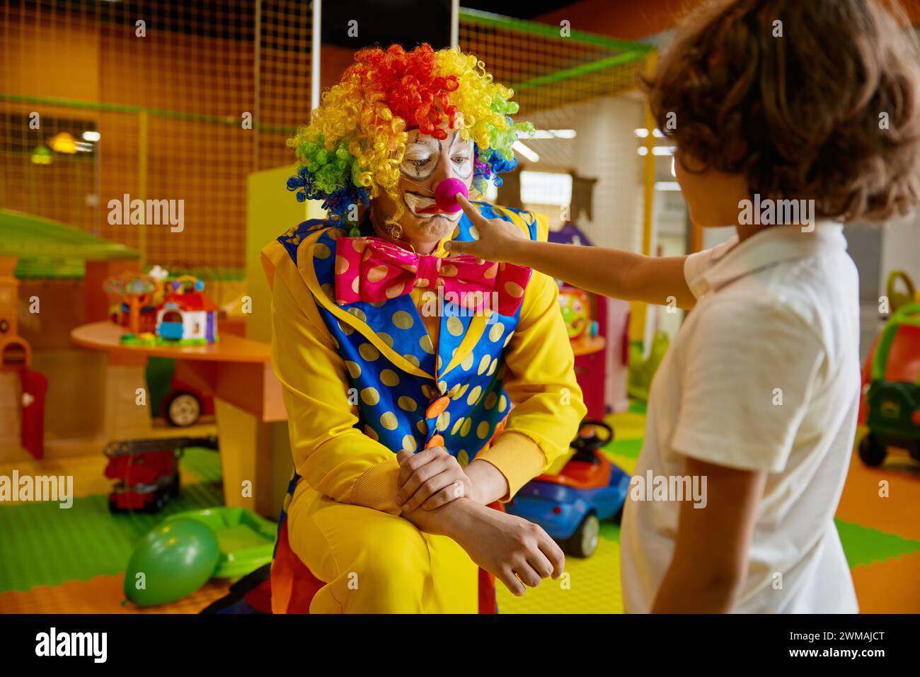 Funny clown animator and boy fooling around playing at indoor playroom ...