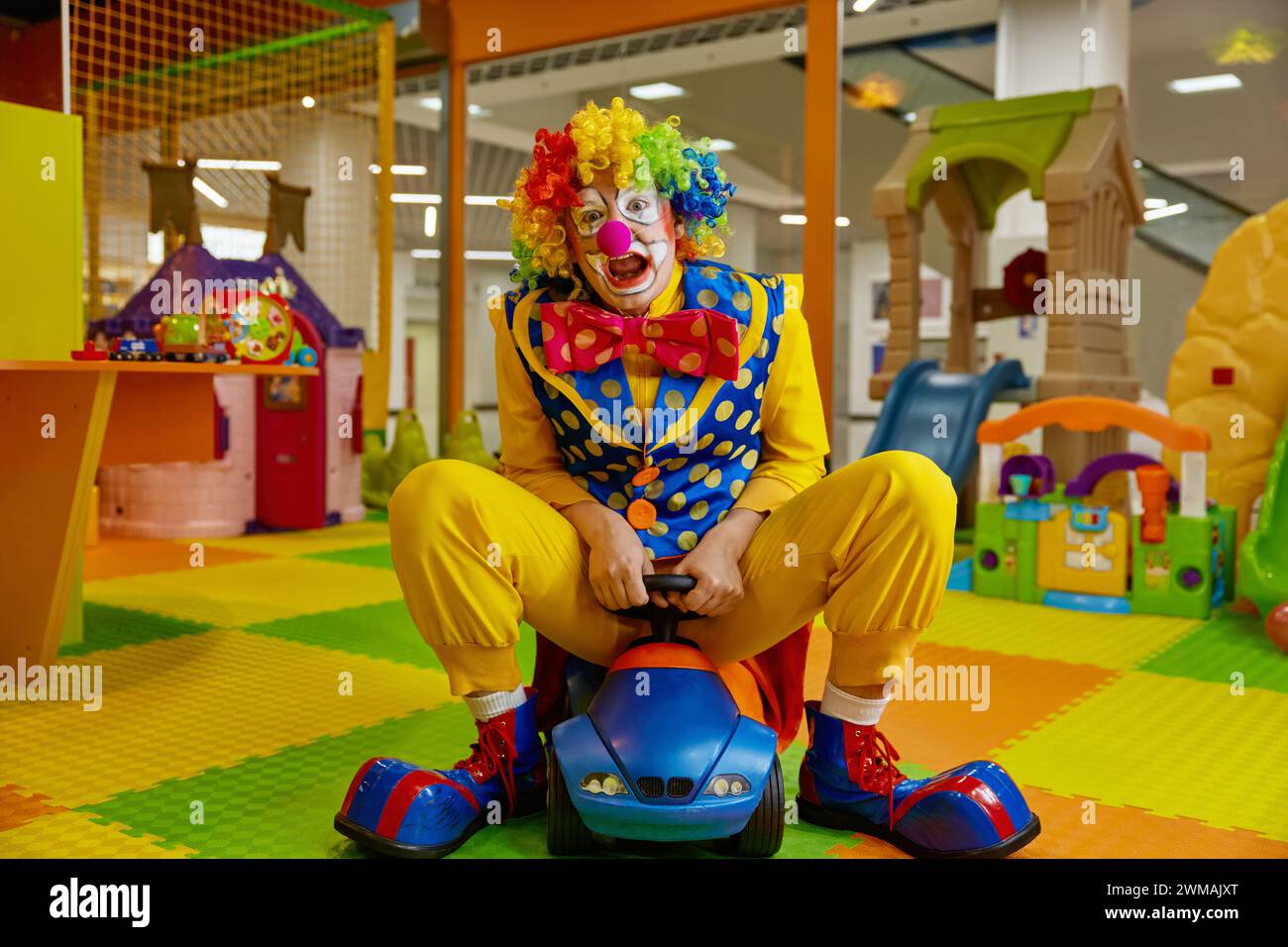 Overjoyed clown having fun riding toy car at playroom Stock Photo - Alamy