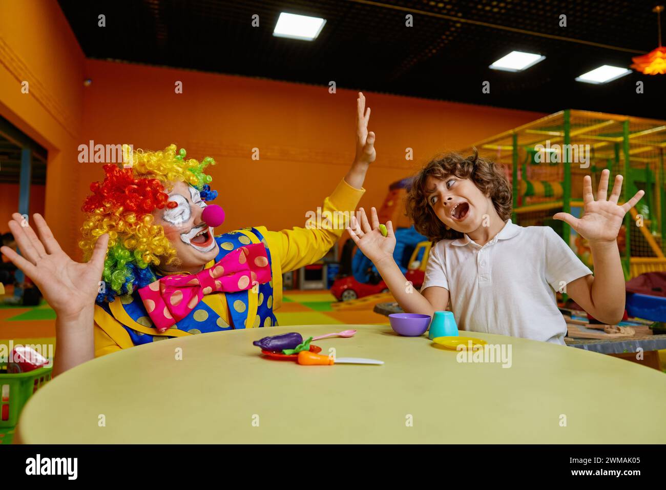 Funny clown and boy fooling around while drinking tea from toy cup ...