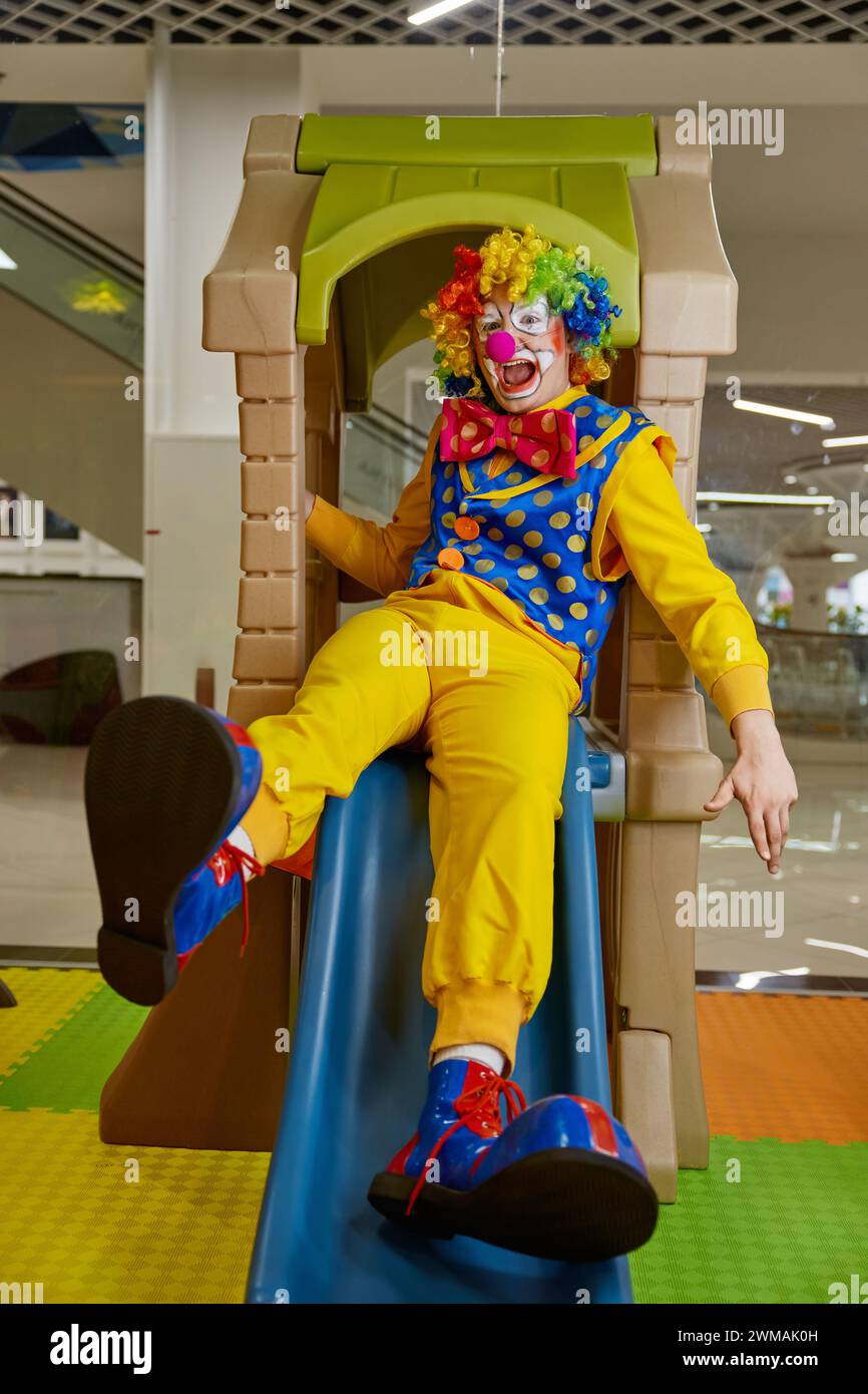 Overjoyed clown in colorful costume sliding down at playroom Stock ...