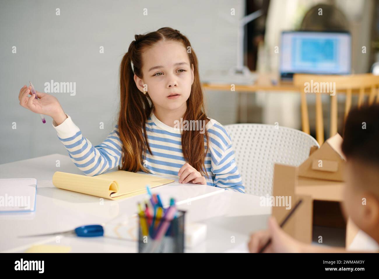 Serious schoolgirl taking to classmate and writing in copybook Stock ...