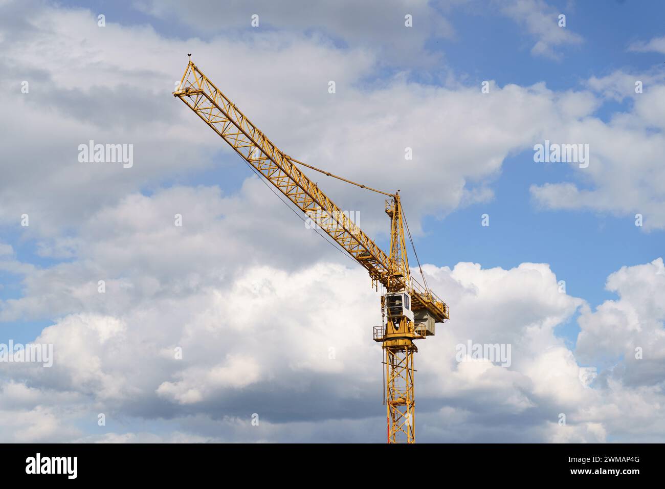 A yellow crane stands tall on a vibrant green field, its long arm ...
