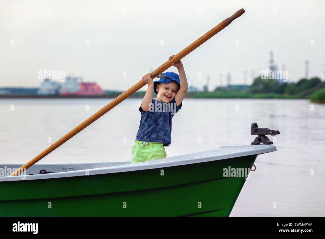 A small cheerful boy is playing in a fishing boat, he is trying to lift ...