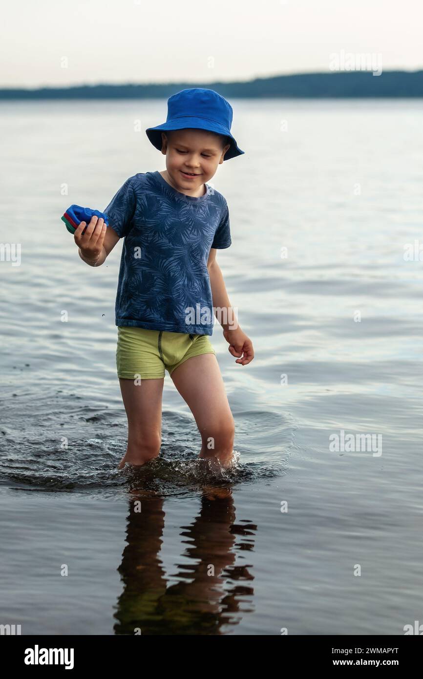 A happy child wading in the calm water of the lagoon in the evening and ...