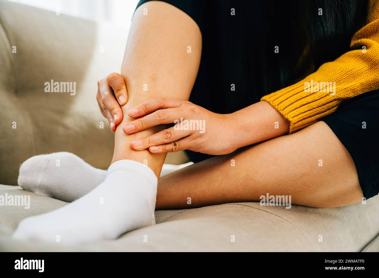 Woman sitting on sofa holds her ankle injury expressing pain Stock ...