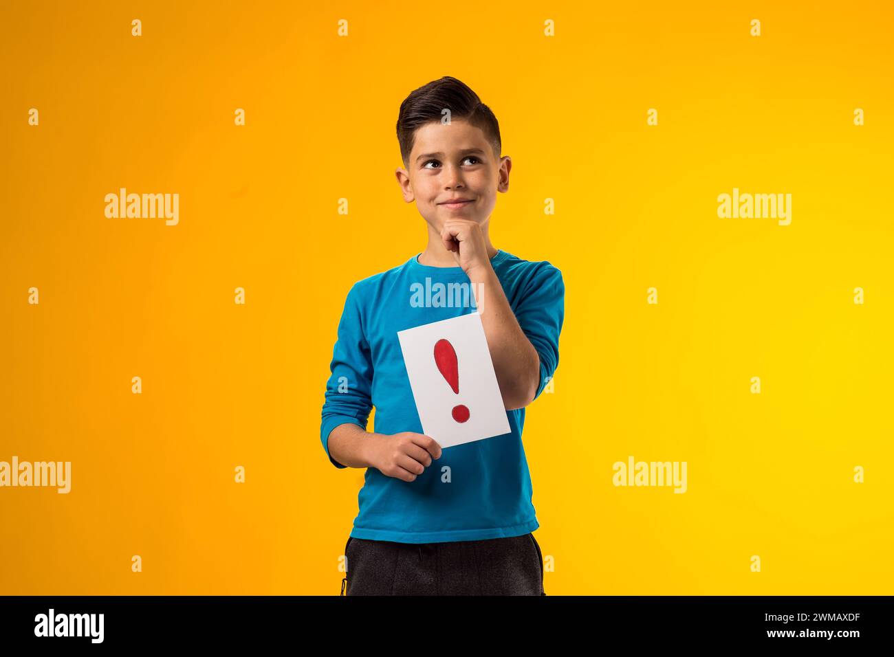 Portrait of thoughtful kid boy holding exclamation point card and ...
