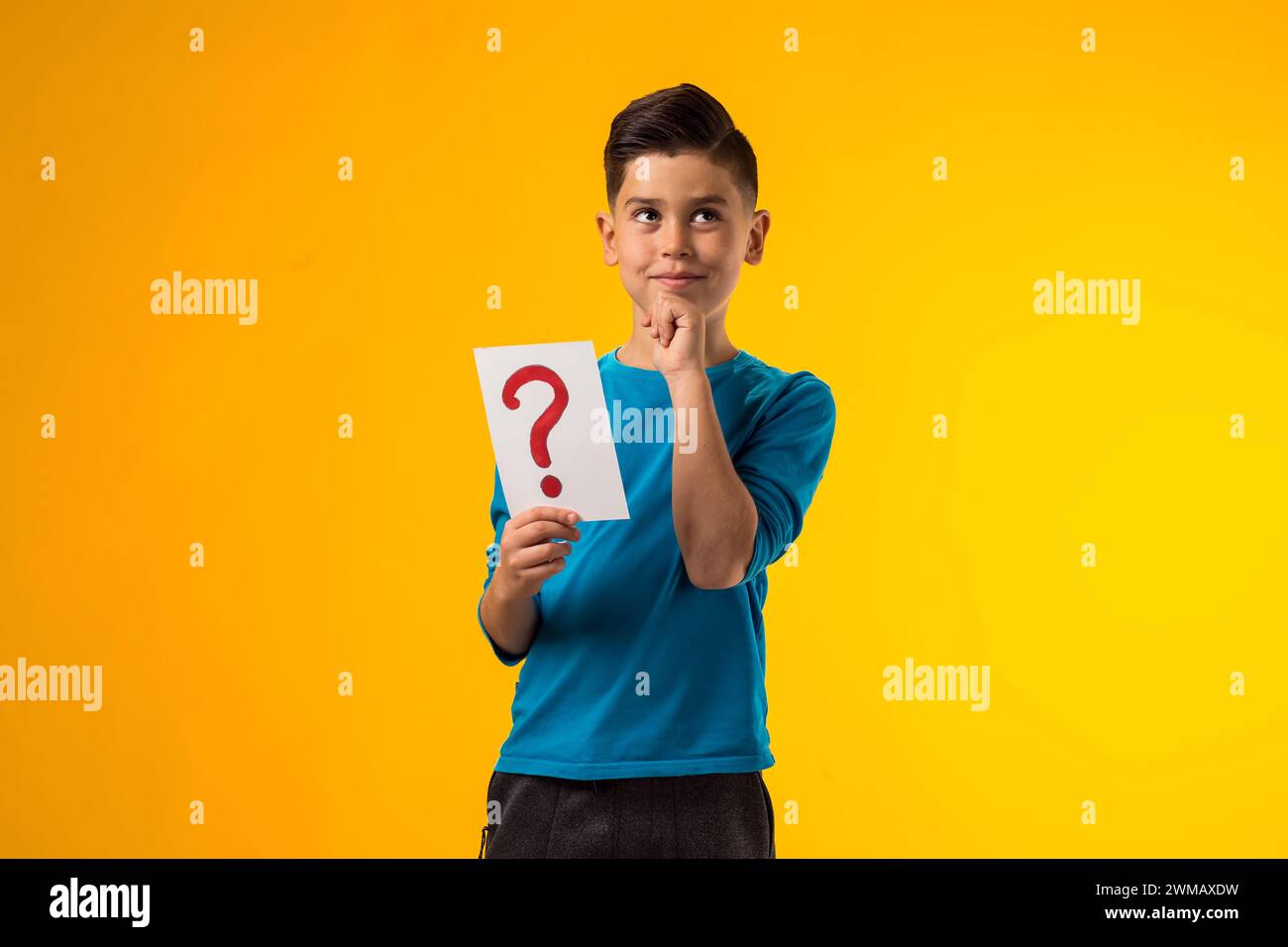 Portrait of thoughtful kid boy holding question mark card in hand and touching his chin ...