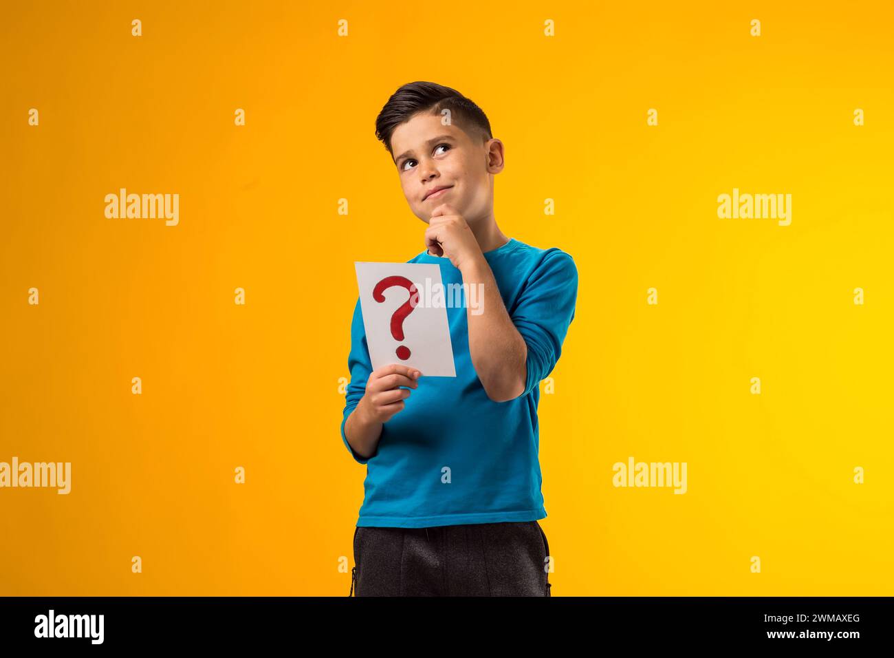 Portrait of thoughtful kid boy holding question mark card in hand and ...