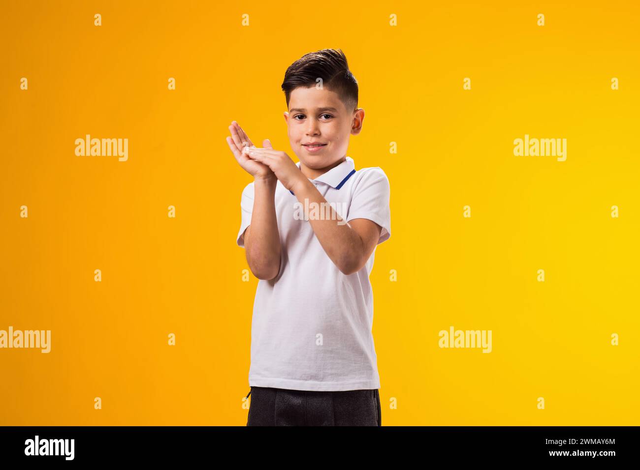 Portrait of smiling kid boy clapping his hands over yellow background ...