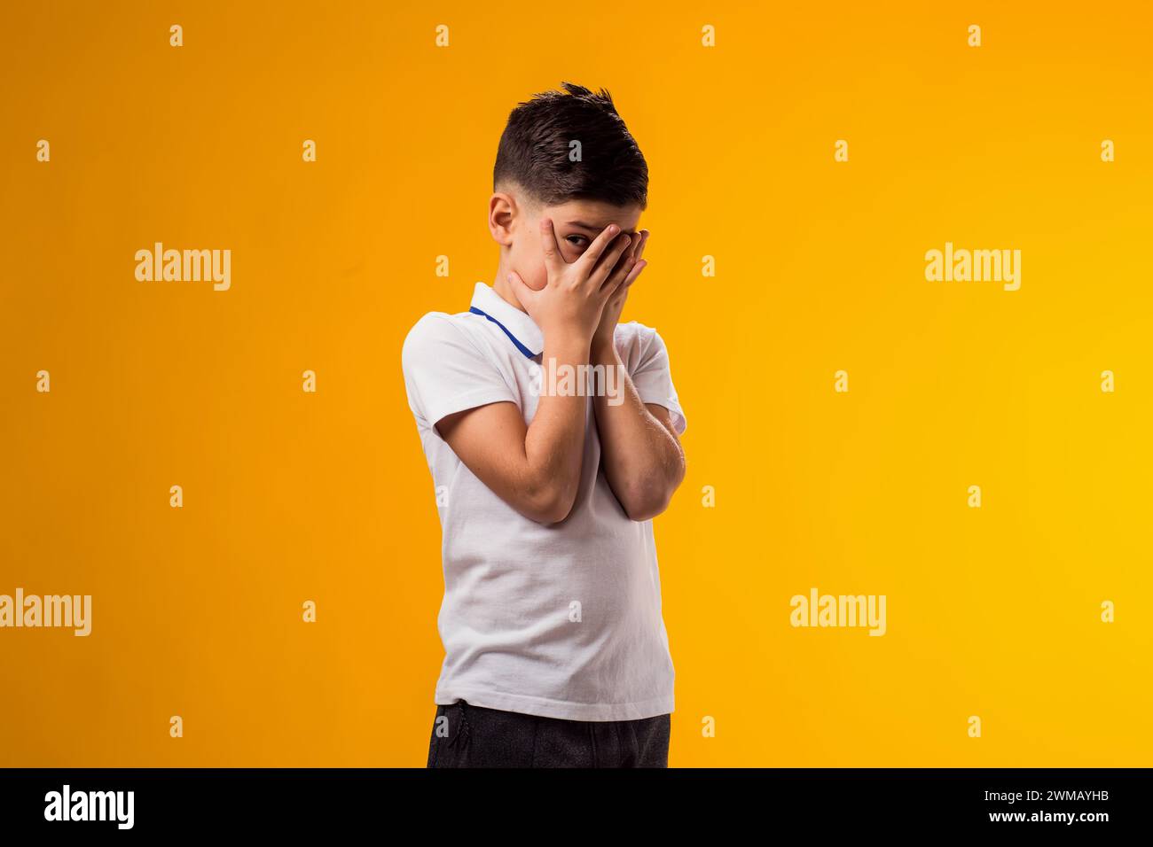 Portrait of upset kid boy covering face with palms and looking through ...