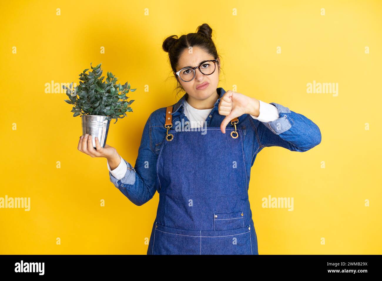 Young caucasian gardener woman holding a plant isolated on yellow ...
