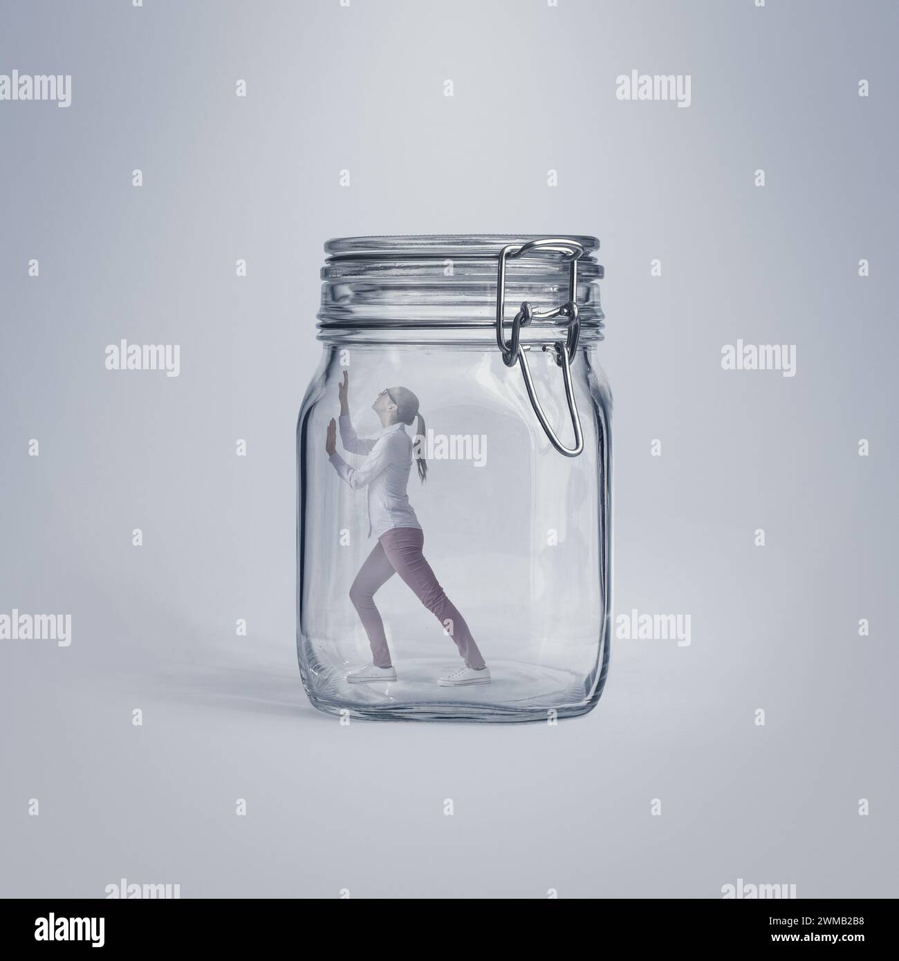 Scared young woman trapped in a huge glass jar, she is desperate and ...