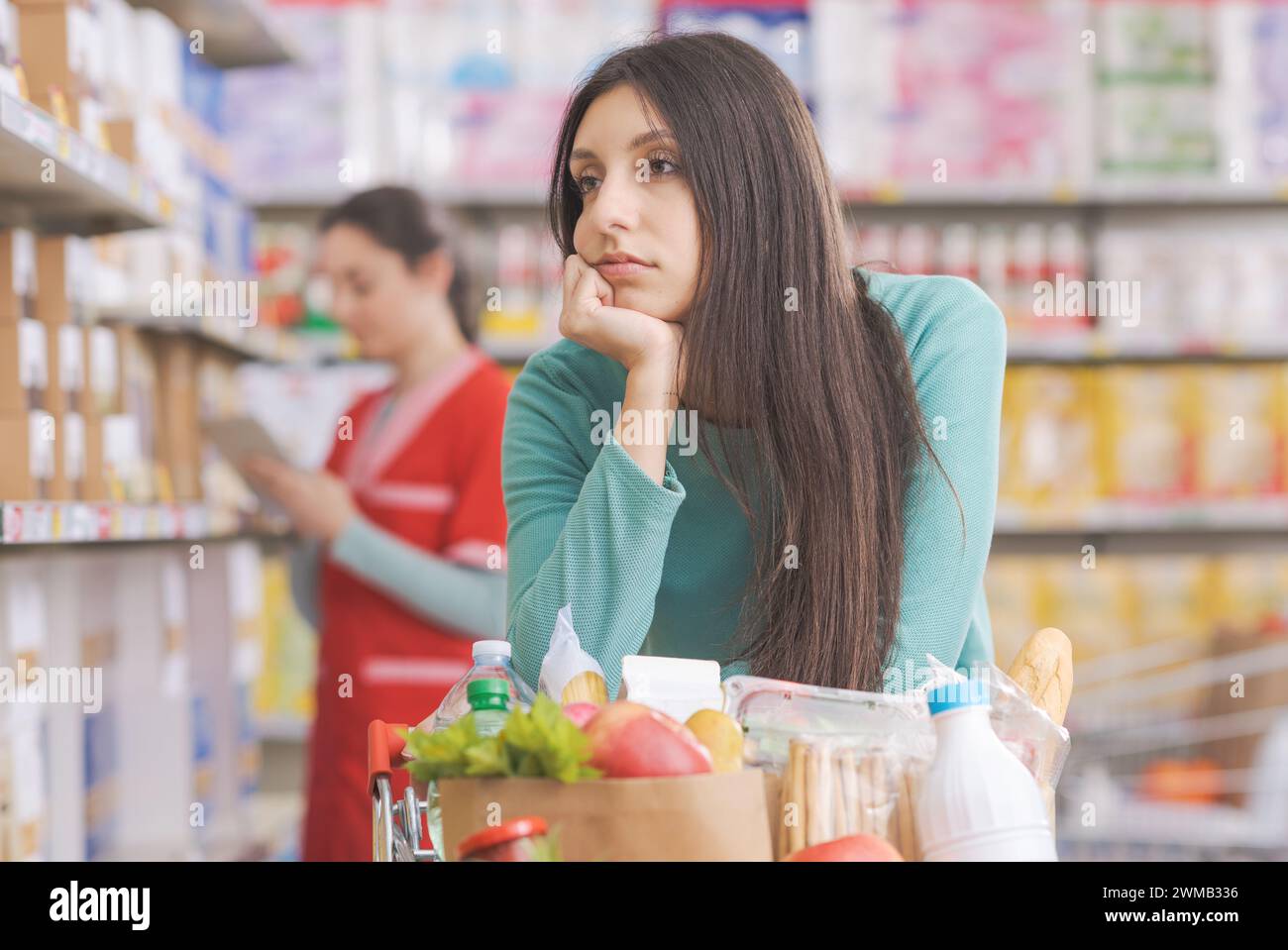 Bored young woman leaning on the shopping cart at the grocery store ...