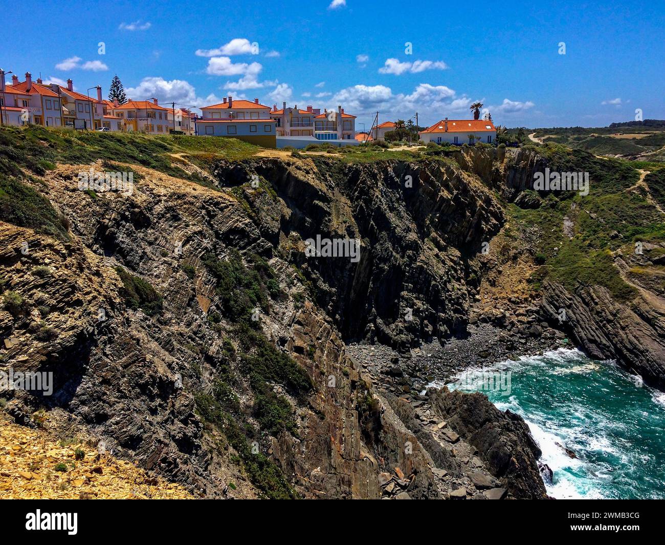 The image shows a coastal town with orange-roofed buildings on rugged ...