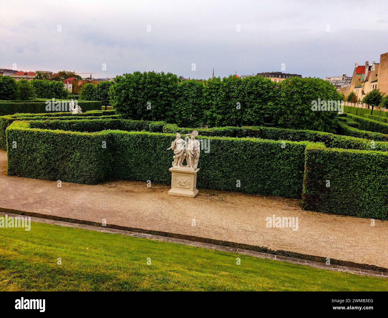 A garden with manicured hedges, two white statues, gravel paths, and a ...