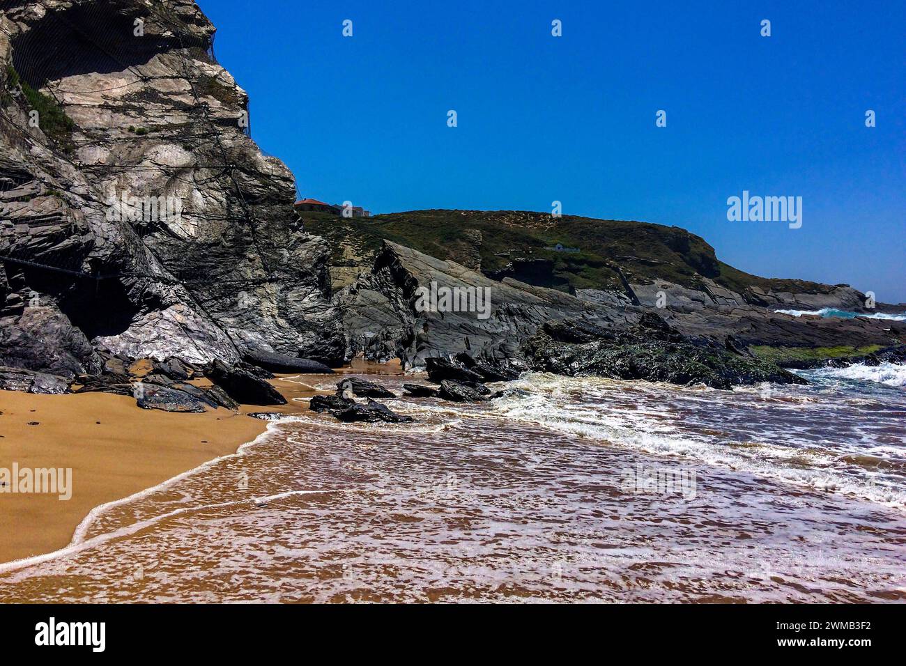 A rocky beach with layered formations, waves crashing, and a cliff ...