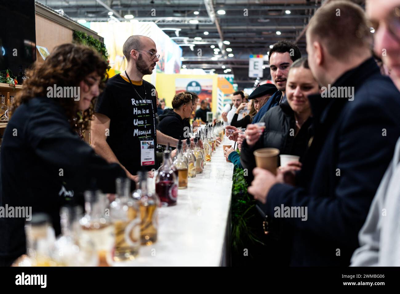 People dripping alcohol at a stand with a long line of bottles at the ...