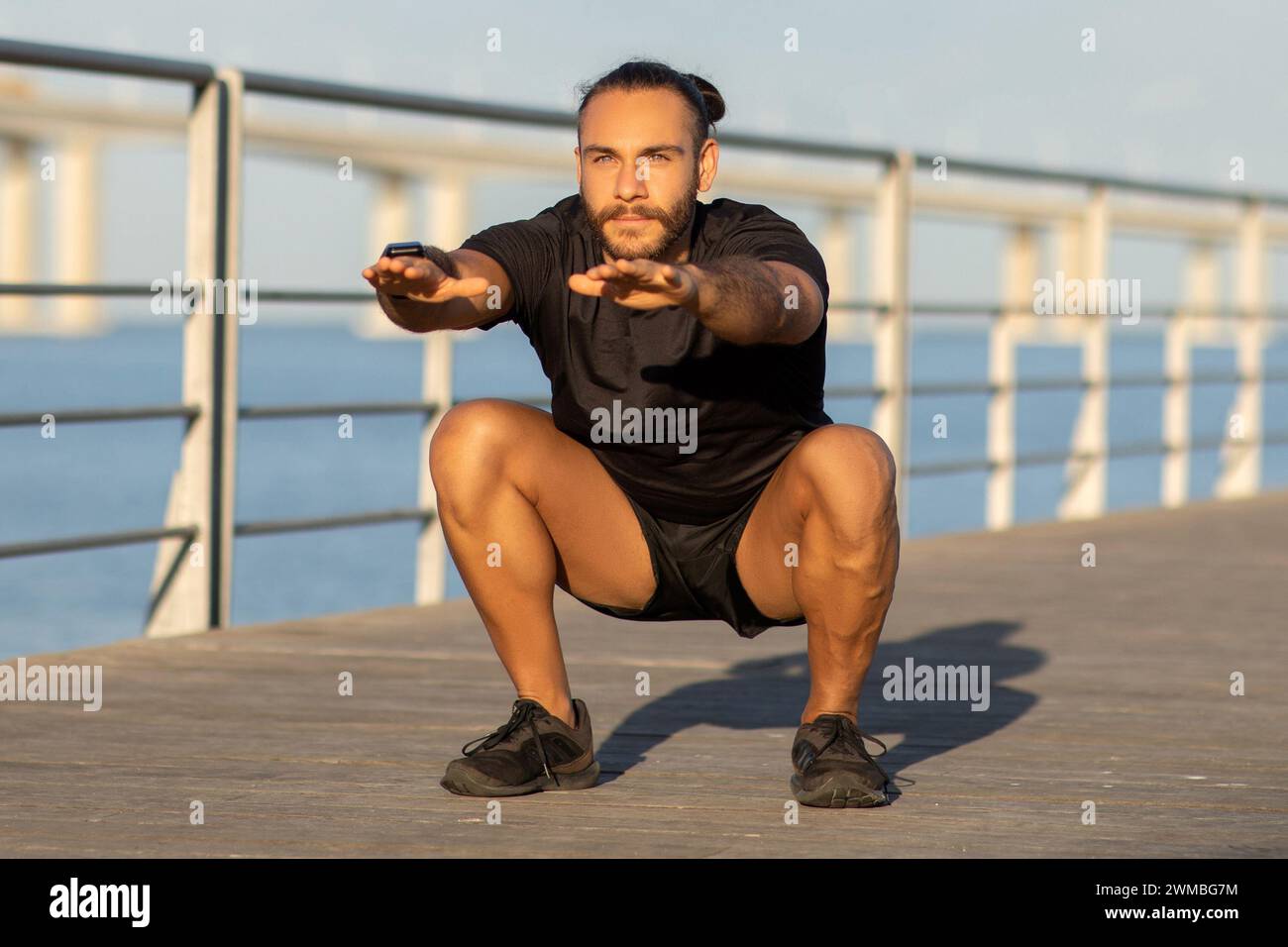 Fit man in black activewear performs squats at seaside outdoor Stock ...