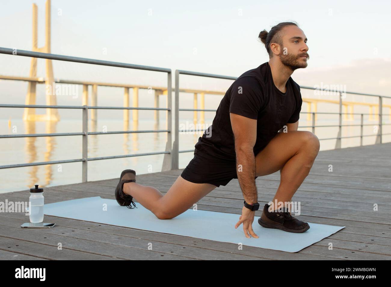 Motivated young man in sporty attire doing leg stretches outside Stock ...