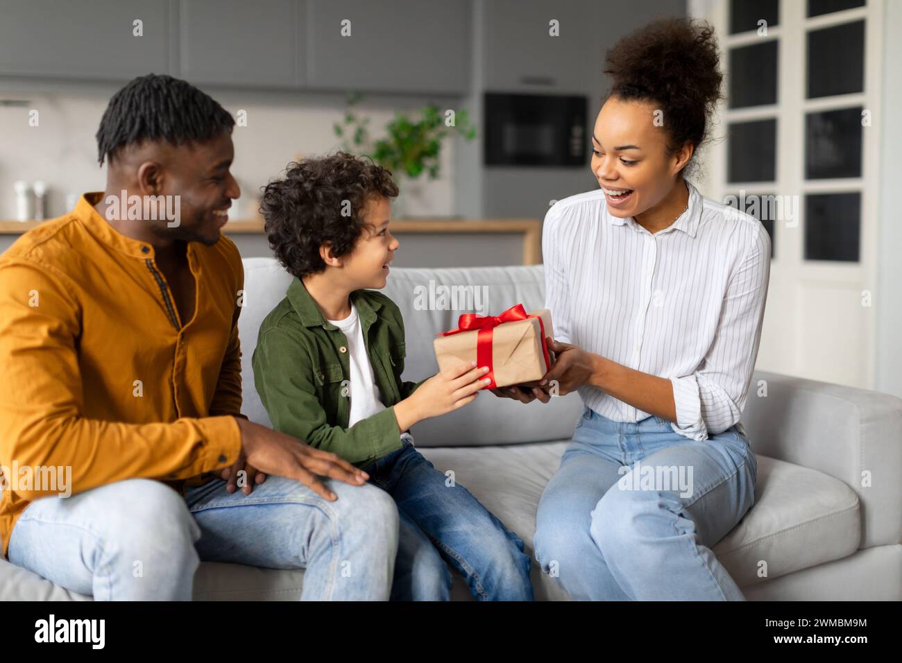 Happy black family sharing gift moment, with child receiving present ...