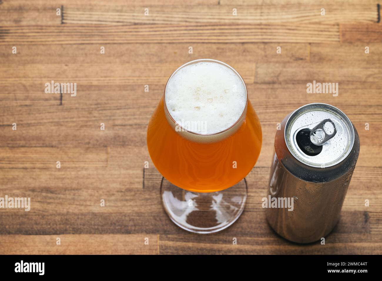 Craft beer in tulip glass next to an open beer can on a rustic wooden ...