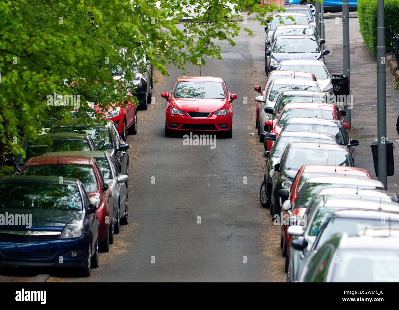 Car in the middle of a road with cars parked on either side, Scotland ...
