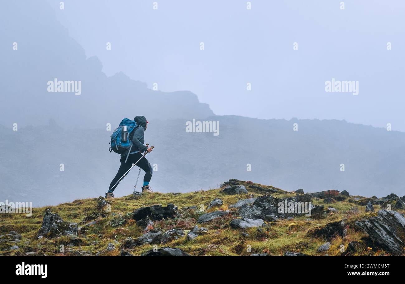 Lonely woman with backpack and trekking poles going by mountain route ...