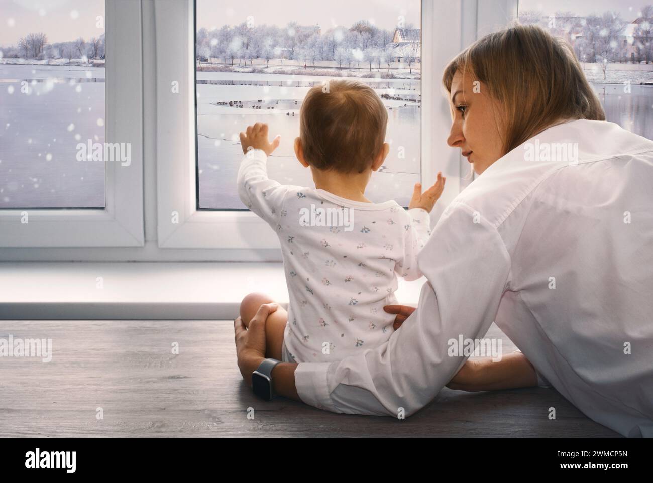 mother and child look out the window at a winter landscape with ...