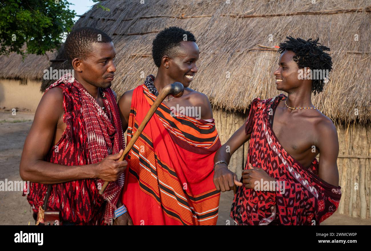 Three male Maasai warrior tribesman wearing shukas chat in their ...
