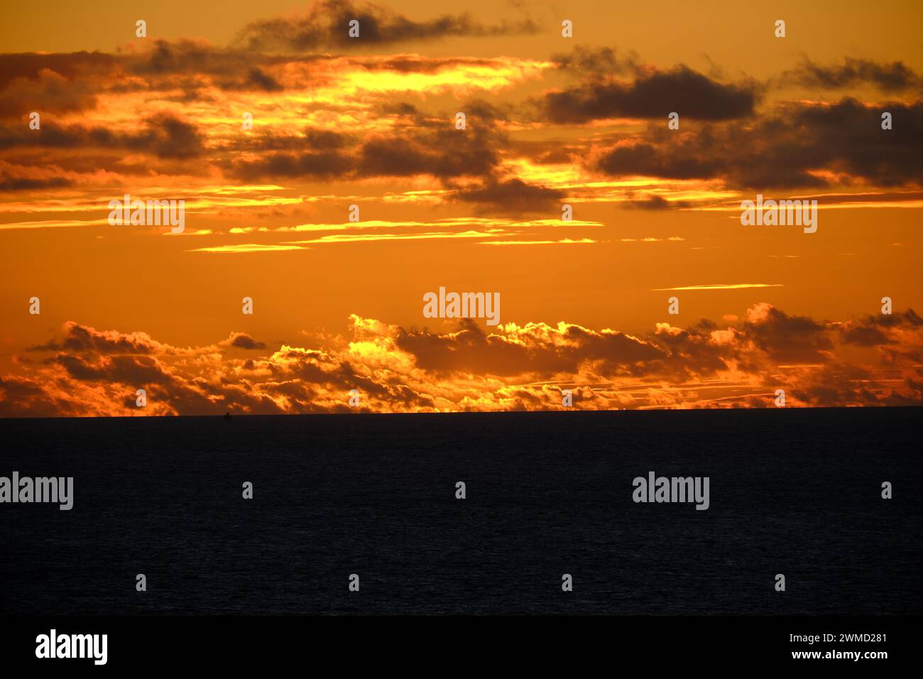 Sun setting over ocean with visible clouds in the sky Stock Photo - Alamy