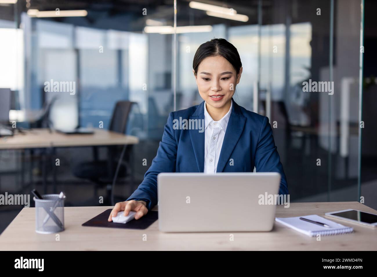 Focused Asian female executive using laptop at her desk in a ...