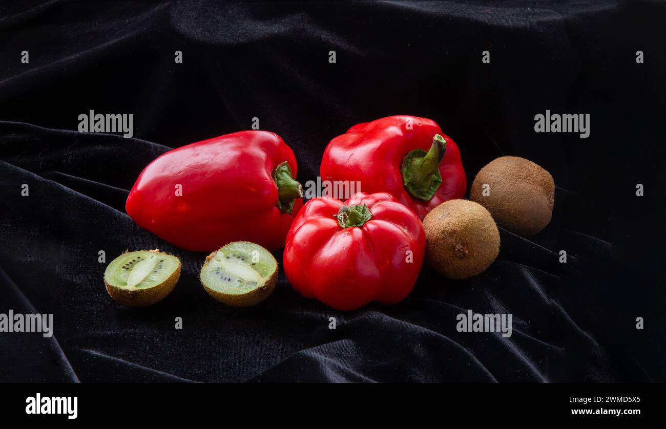 Bright red Bell peppers and kiwi fruits on black fabric. Fruit and ...