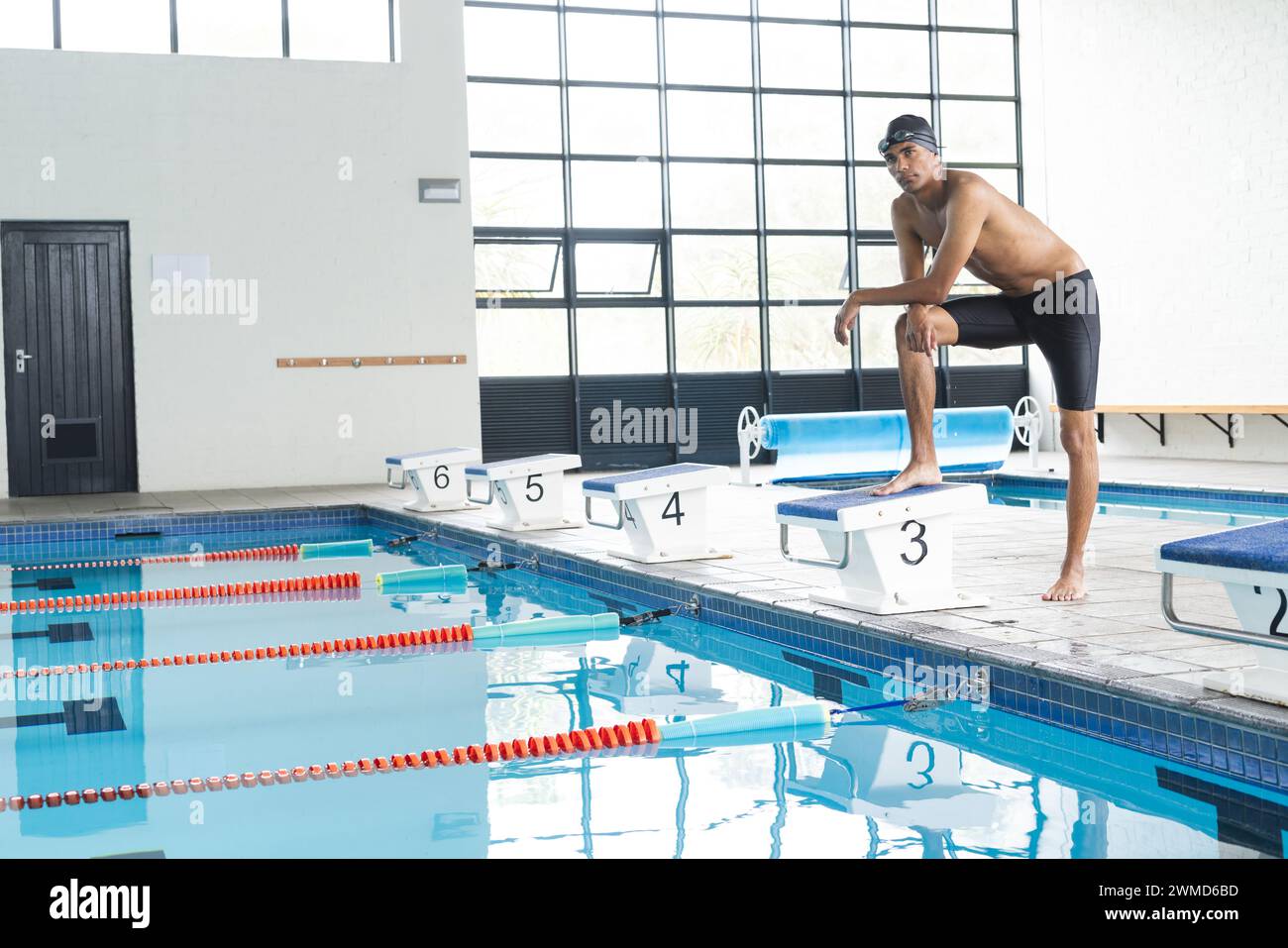 Young biracial male athlete swimmer prepares to dive at an indoor pool ...