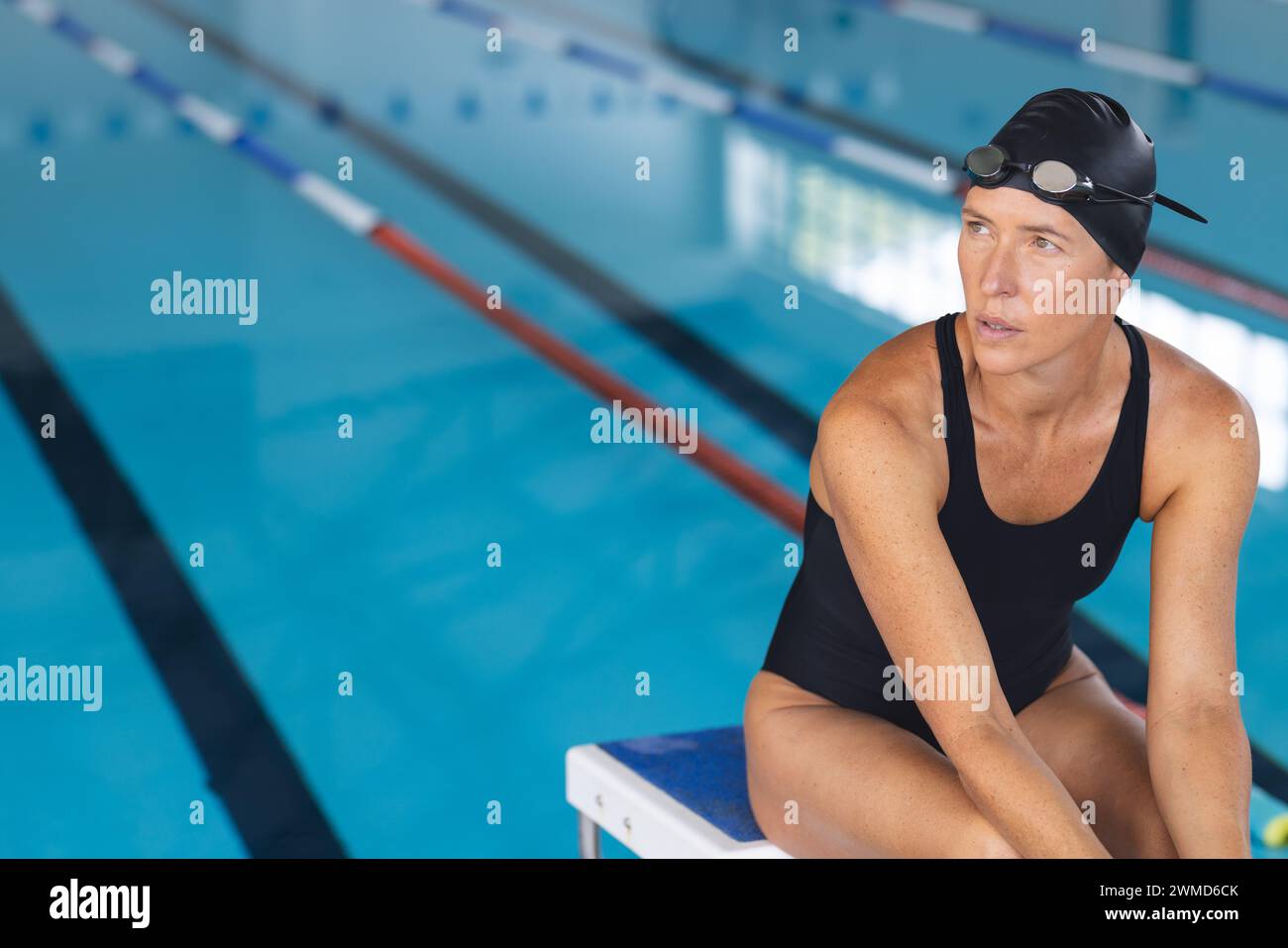 Caucasian female athlete swimmer sits by the poolside, with copy space ...