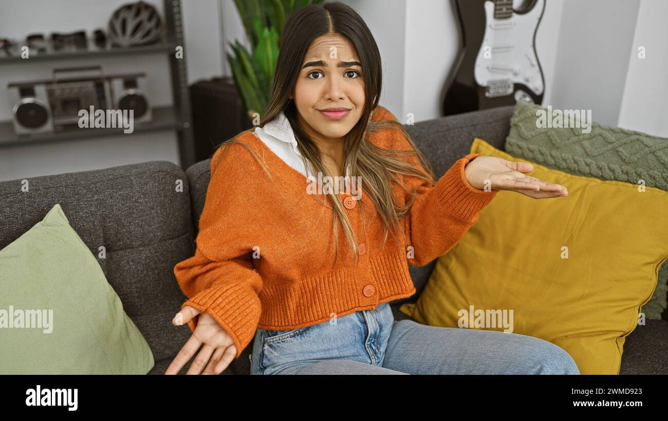 Puzzled young woman with outstretched hand, sitting in a modern living ...