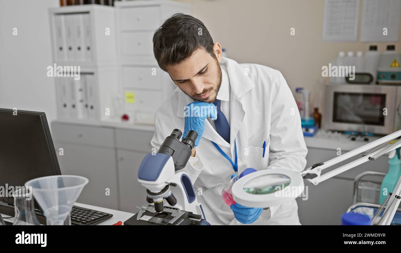 Young hispanic man in lab coat examining a petri dish under a ...