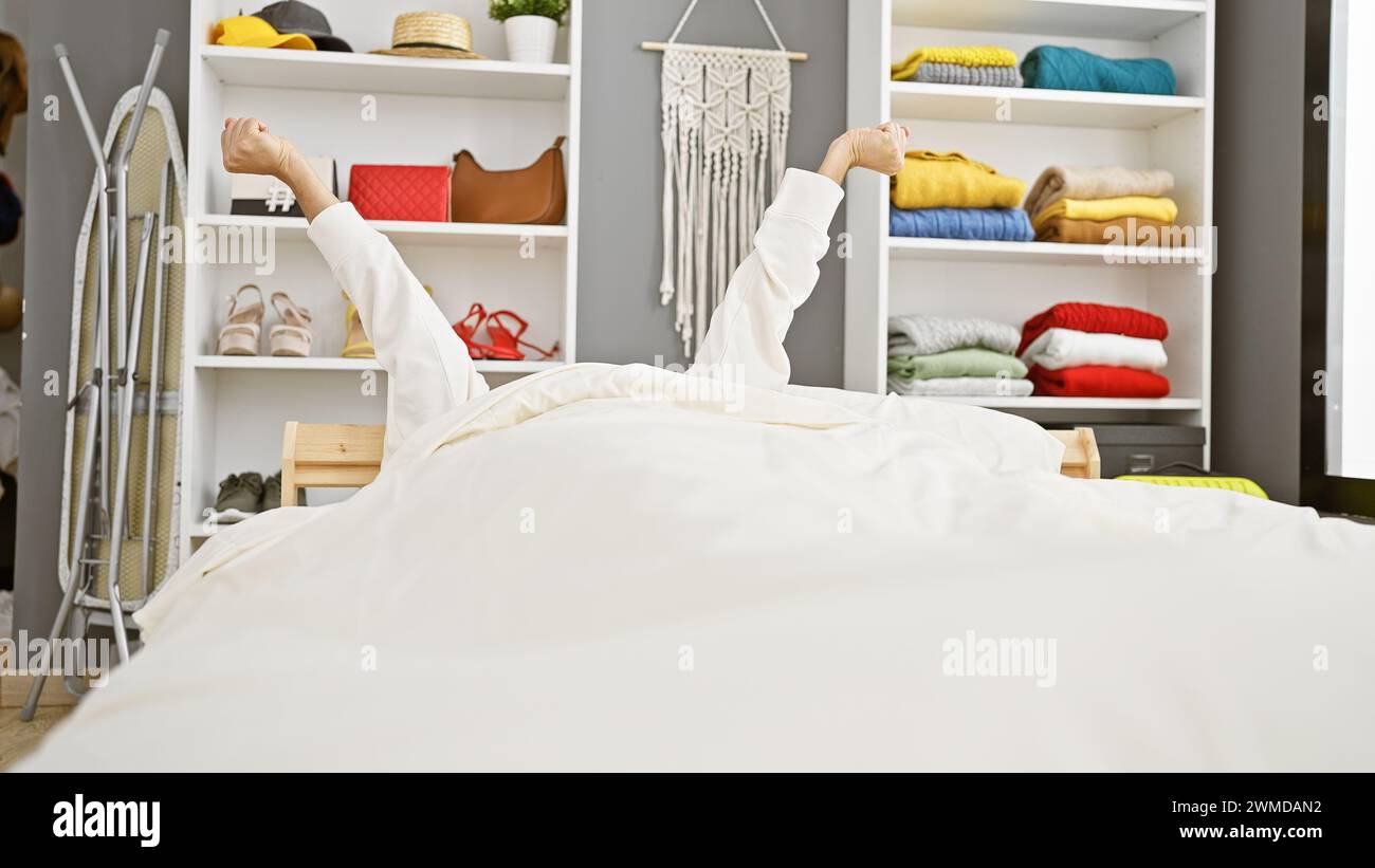 A person stretching in bed with a well-organized wardrobe in a modern ...