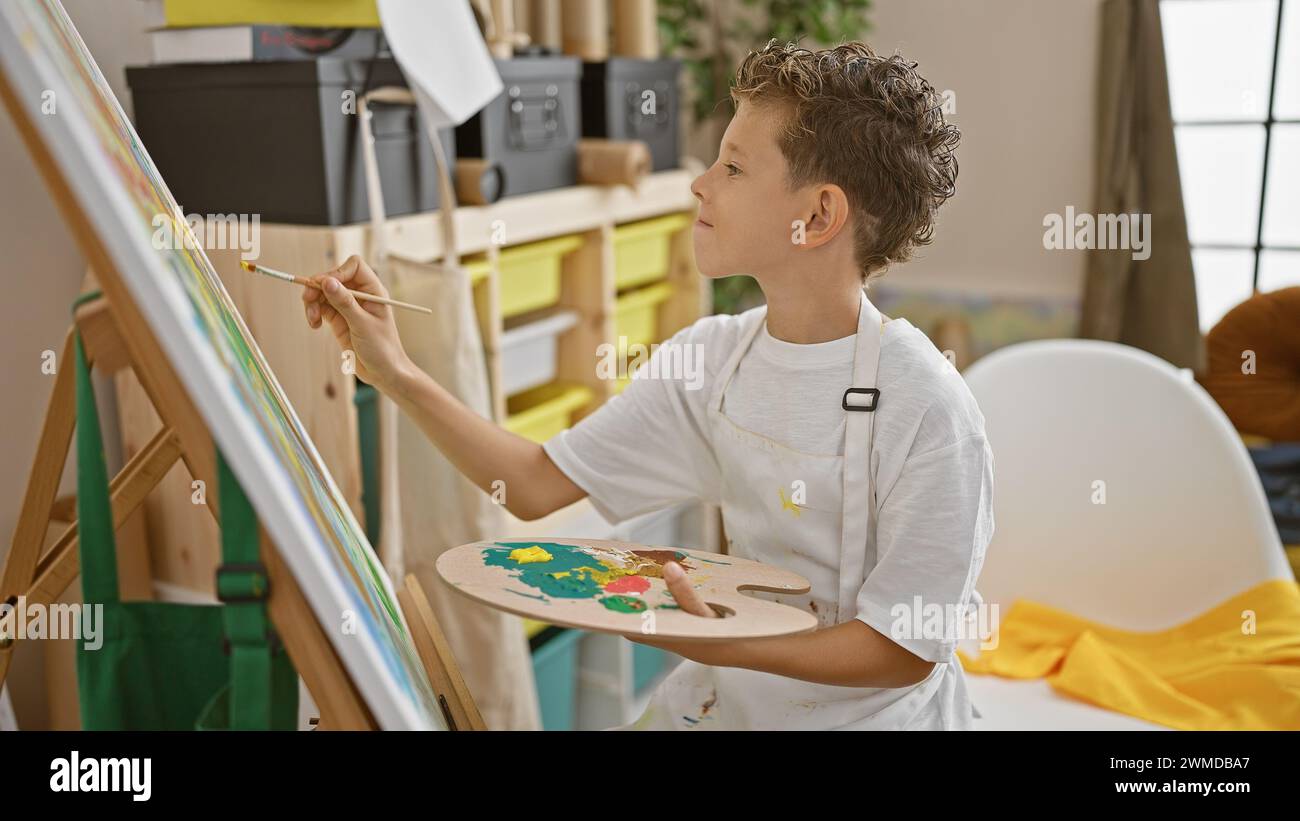 Adorable blond boy artist, confidently smiling as he enjoys drawing at ...