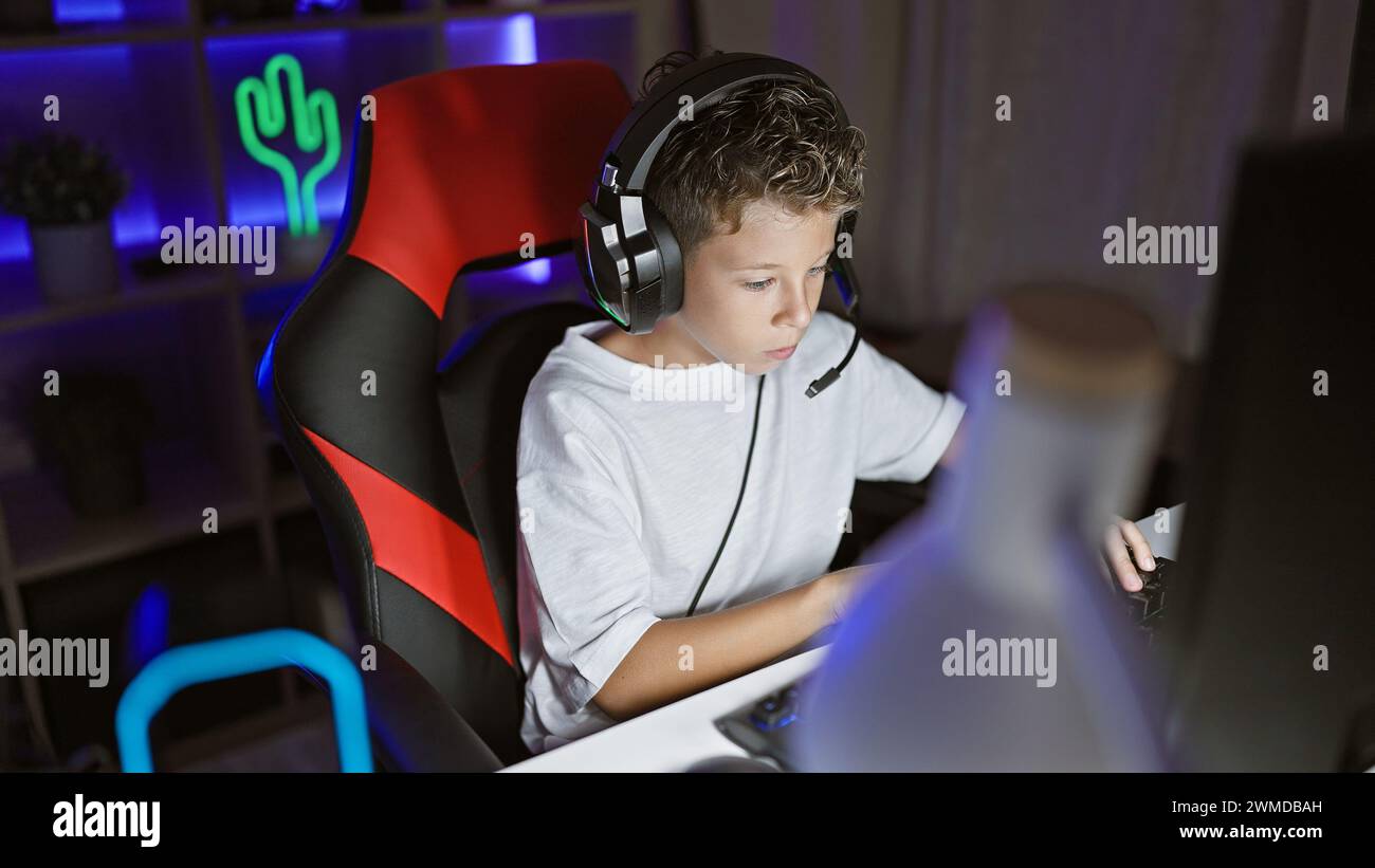 Adorable blond boy streamer, engrossed playing a futuristic video game ...