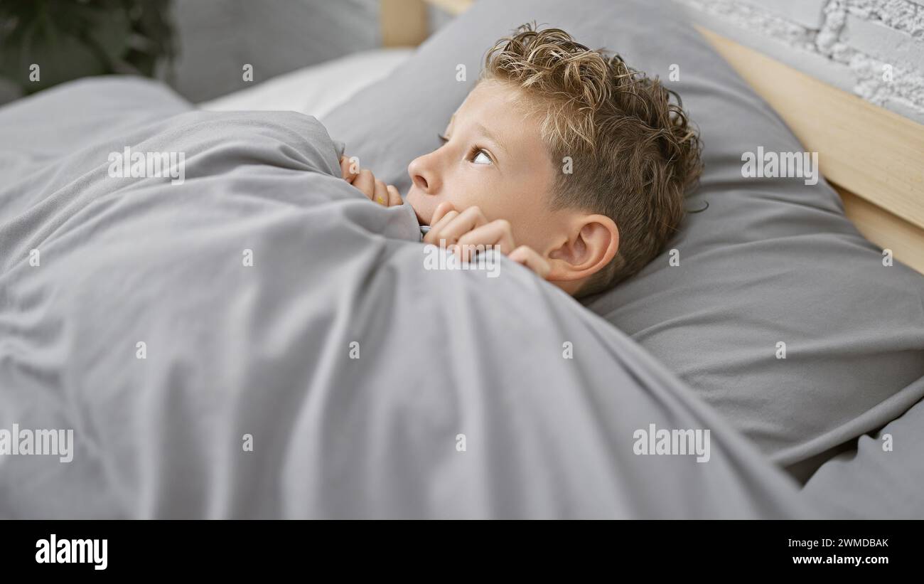 Scared blond boy lying in comfortable bed, covering face with fear in ...