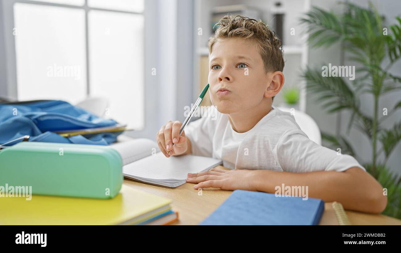Adorable blond boy student, focused on learning, taking notes sitting ...