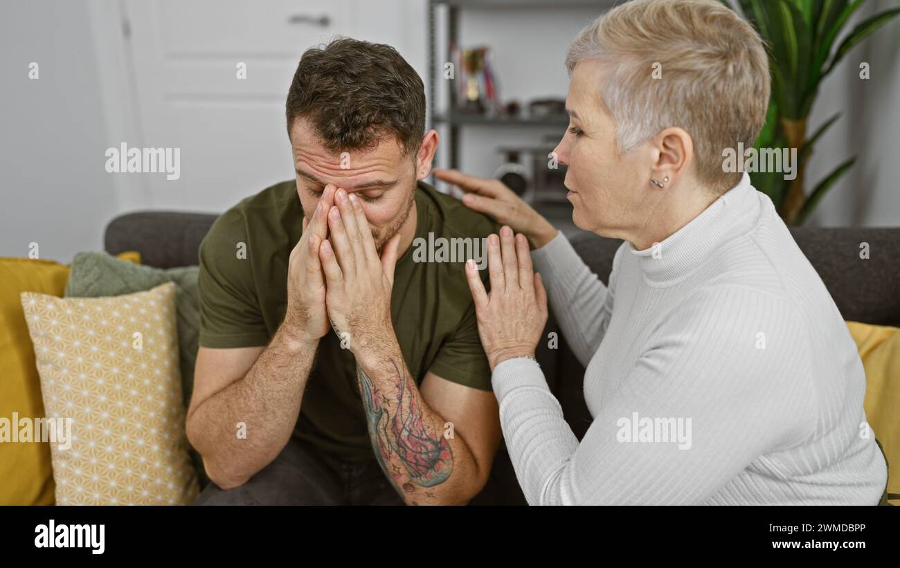 A distressed man consoled by a supportive woman indoors, depicting ...