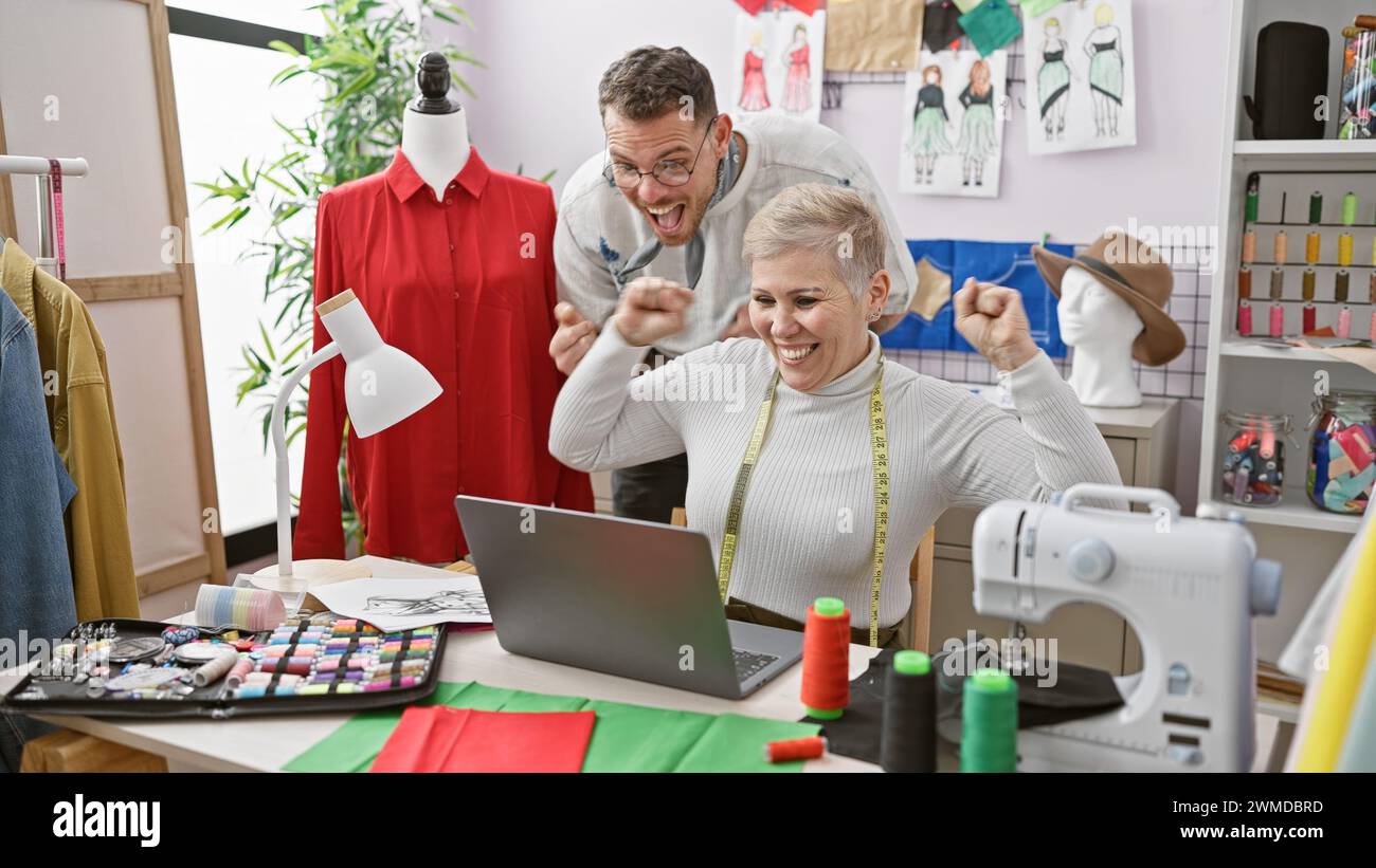 Two tailors, a man and a woman, celebrating a success at a computer in a well-equipped tailoring ...