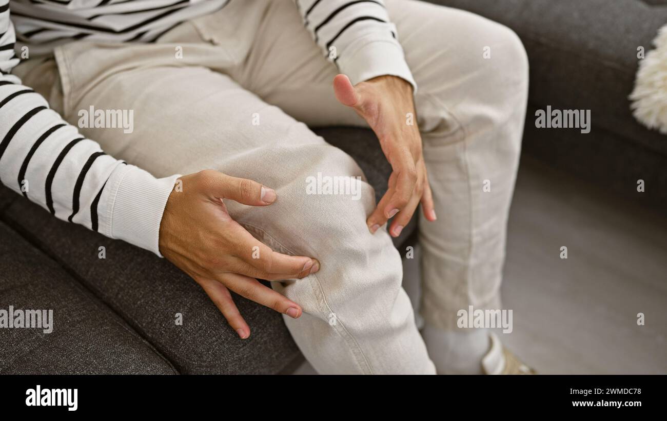 Hispanic man's hands gripping knee in pain, sitting on comfy living ...
