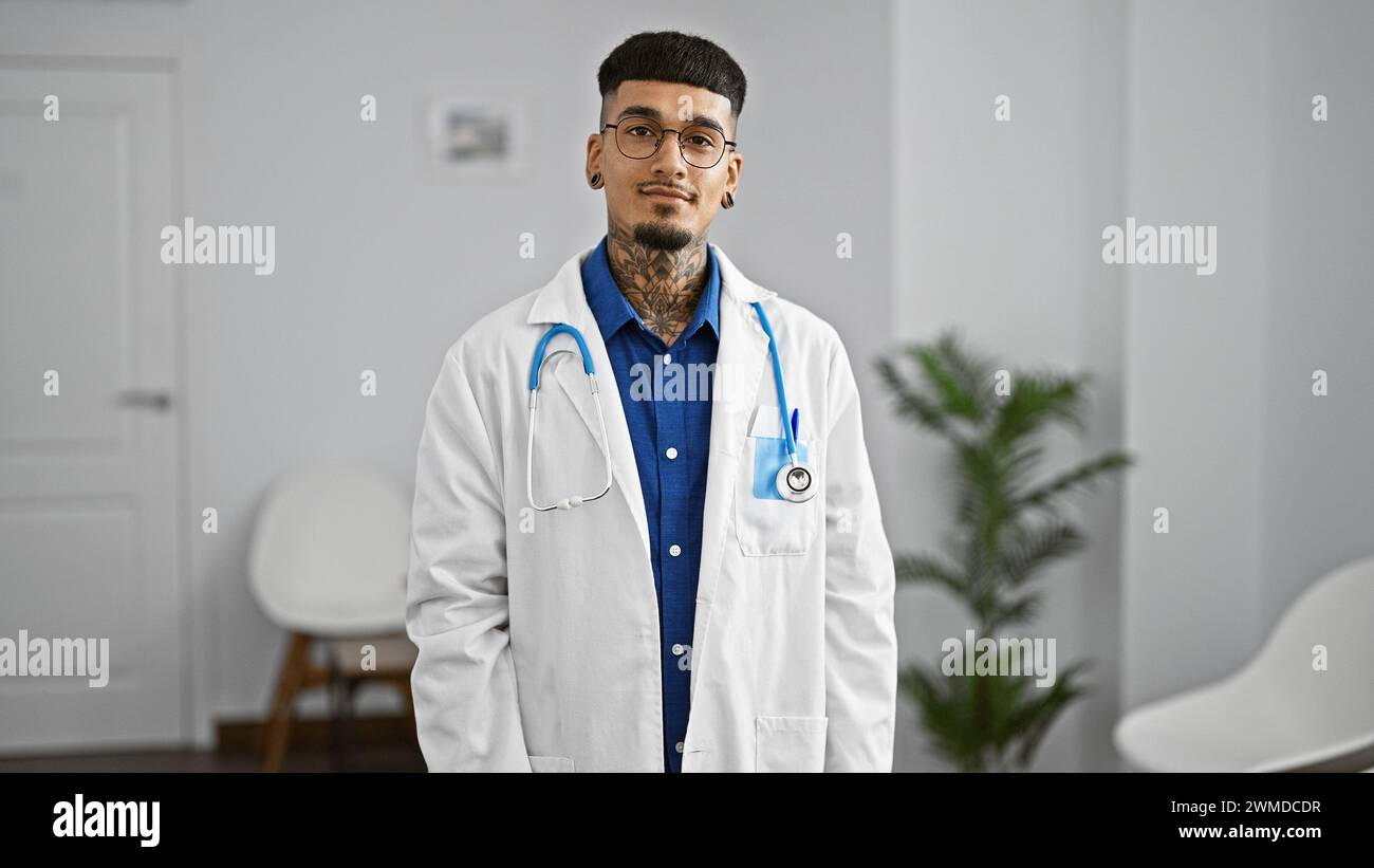 Focused young latin man doctor, sporting tattoo and glasses, stands in ...