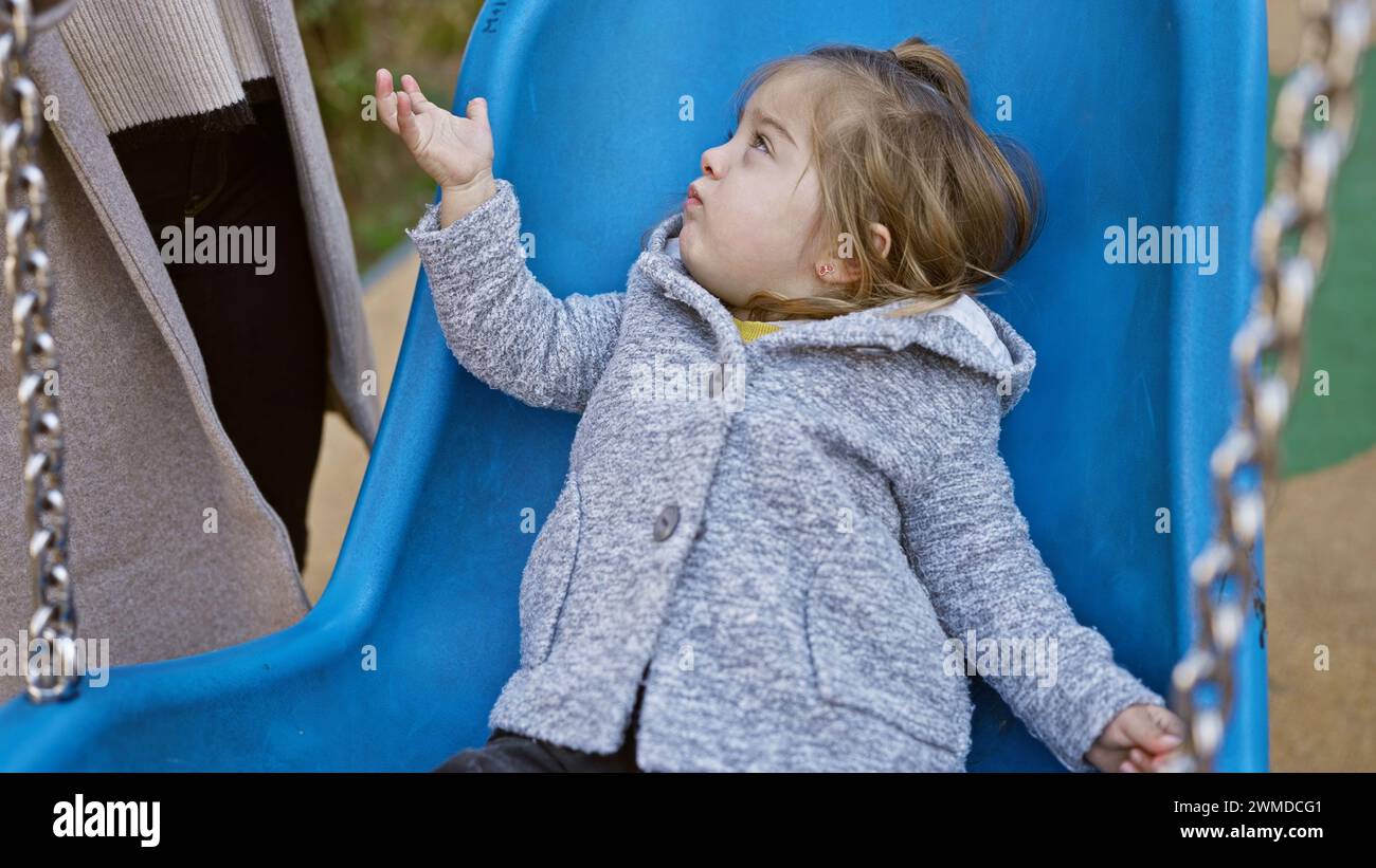 Little girl enjoying a slide in a park clad in a cozy gray coat on a ...