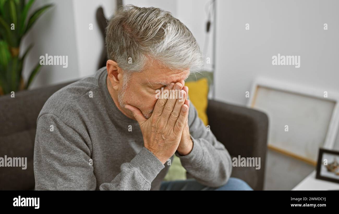 A distressed senior man indoors covering face with hands, showing signs ...
