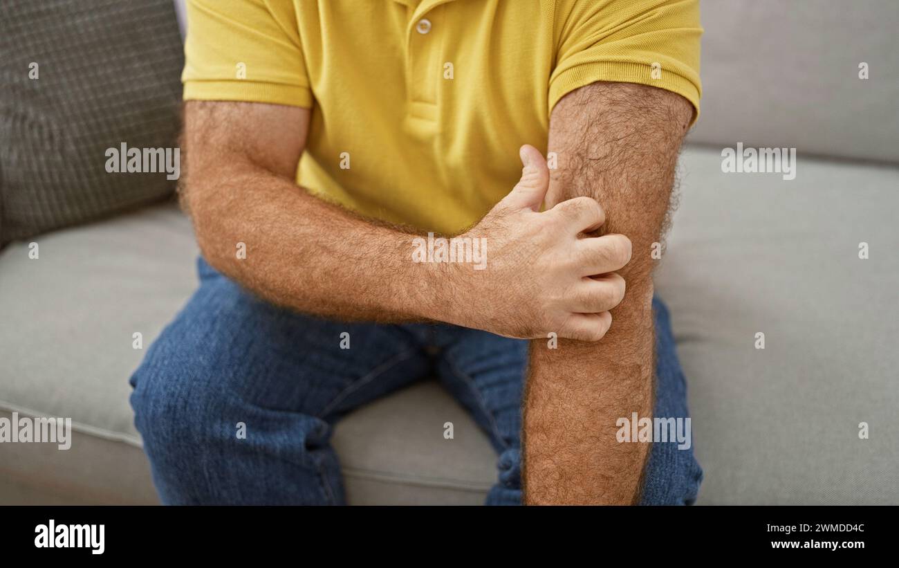 Handsome middle-aged caucasian man sitting on sofa at home, scratching ...