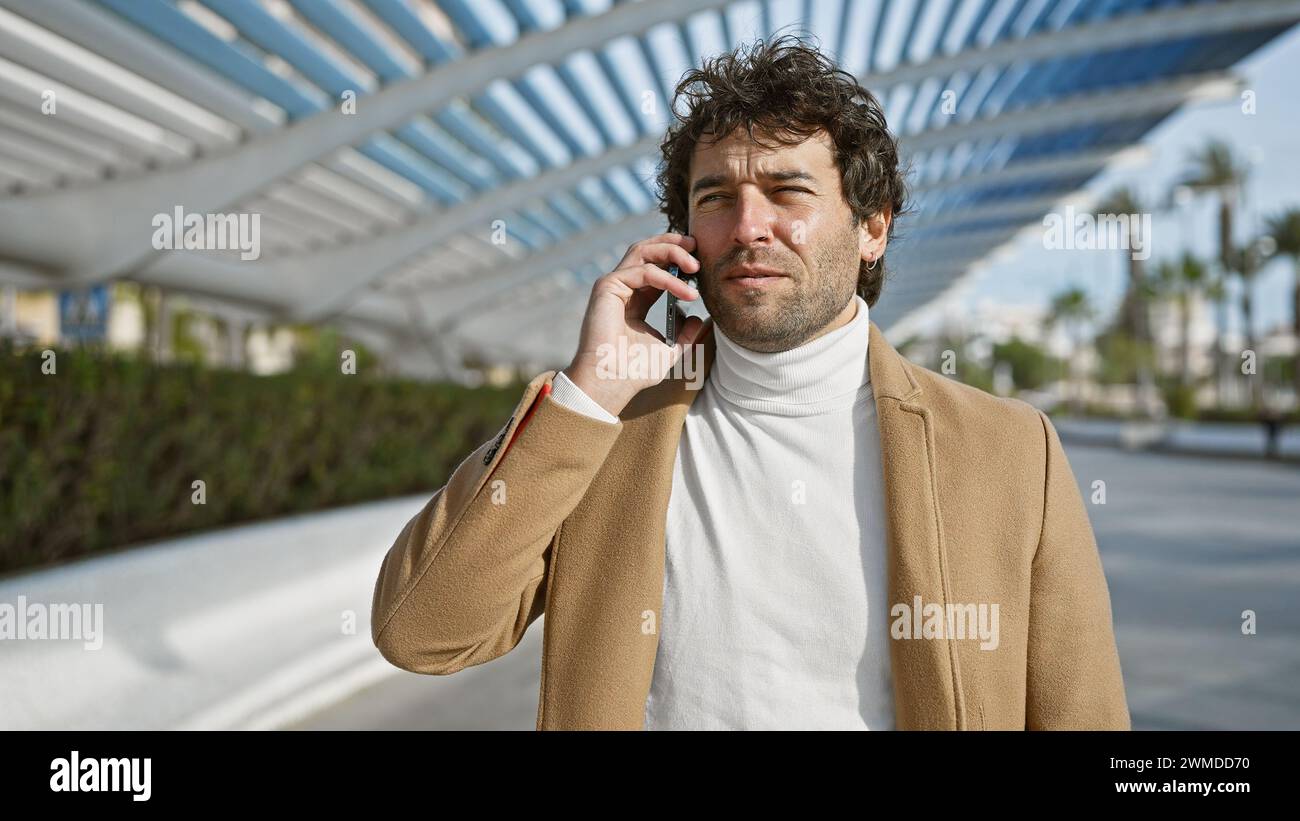 Handsome young hispanic man with beard talking on phone outdoor in city park wearing coat Stock ...