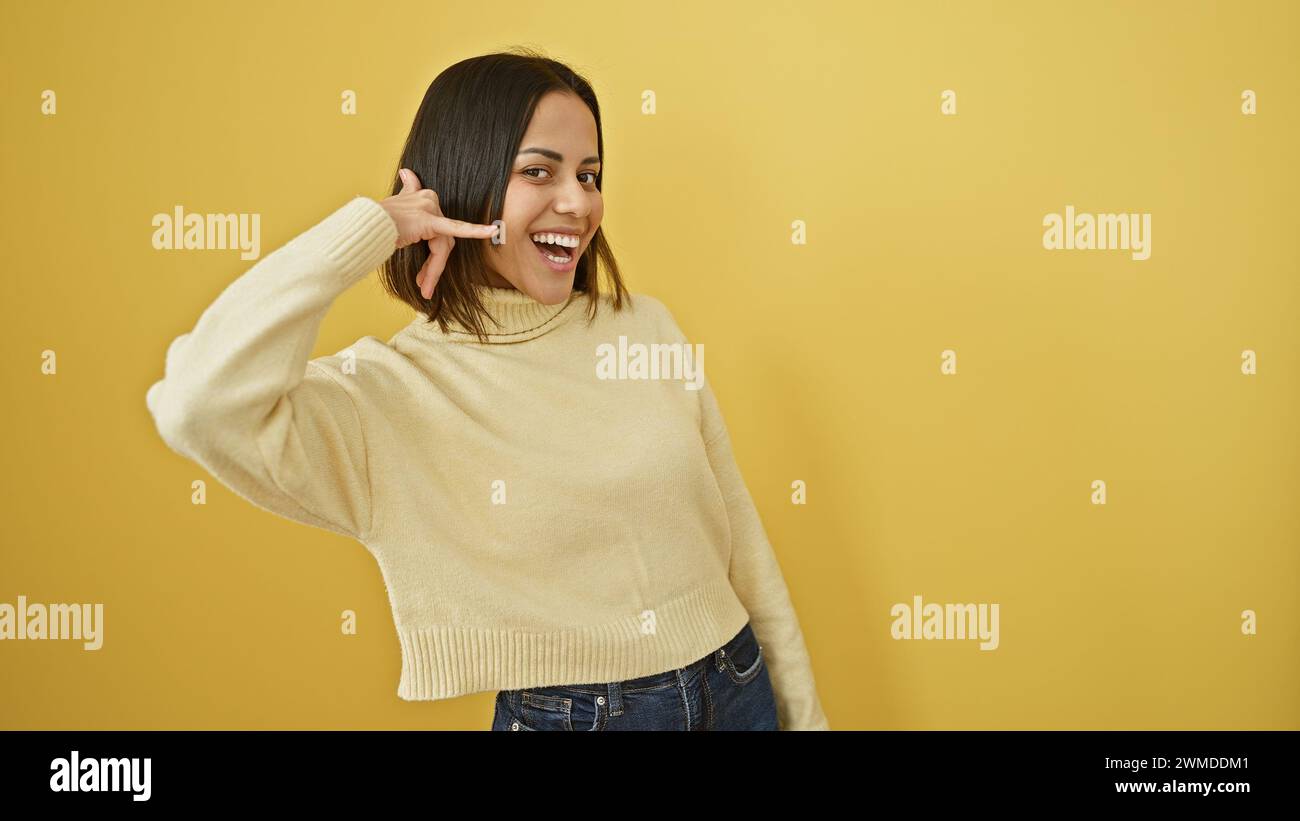 A young hispanic woman makes a call me gesture against a yellow ...